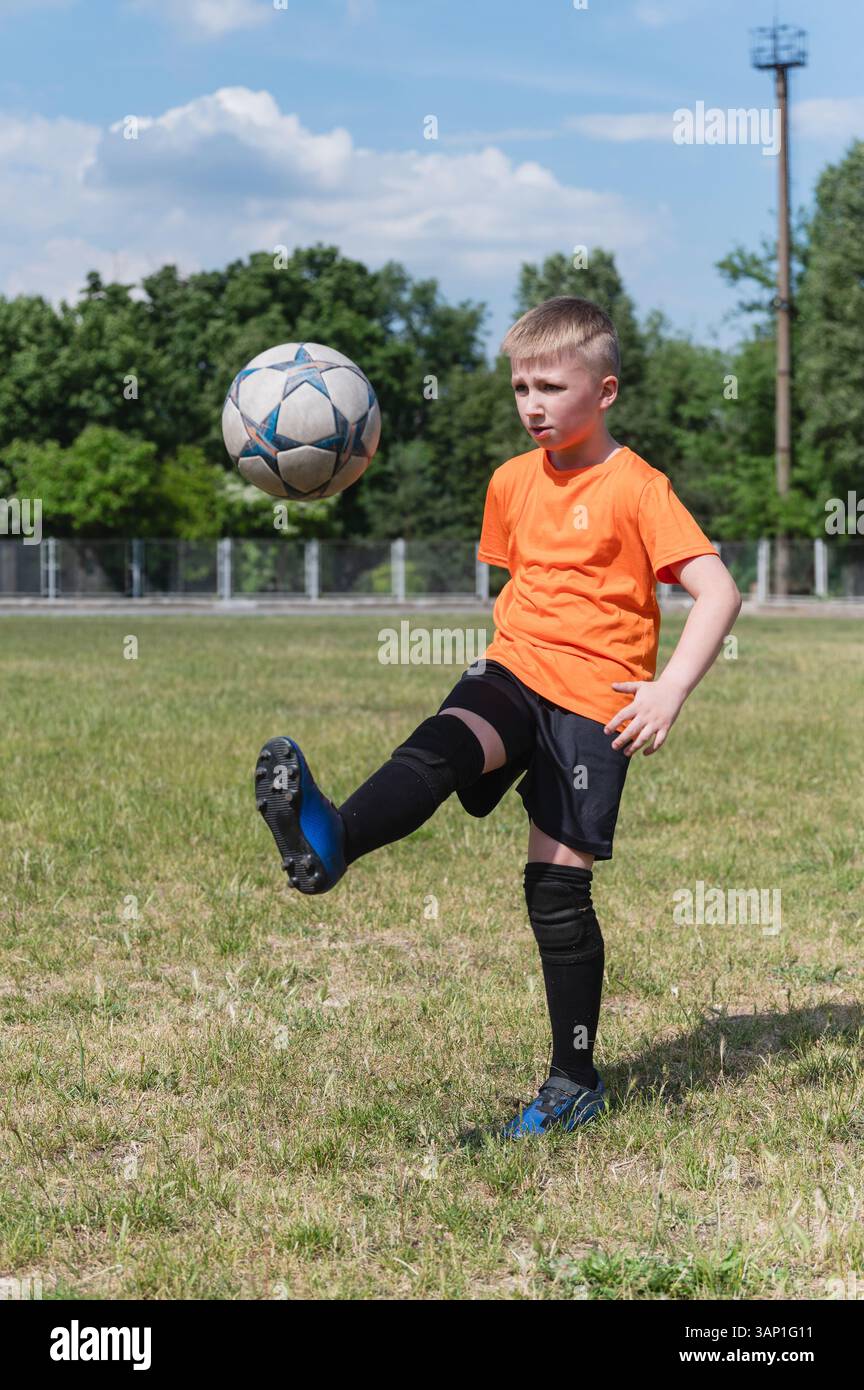 Boy in orange shirt performing kick-ups with a soccer ball on a sunny ...