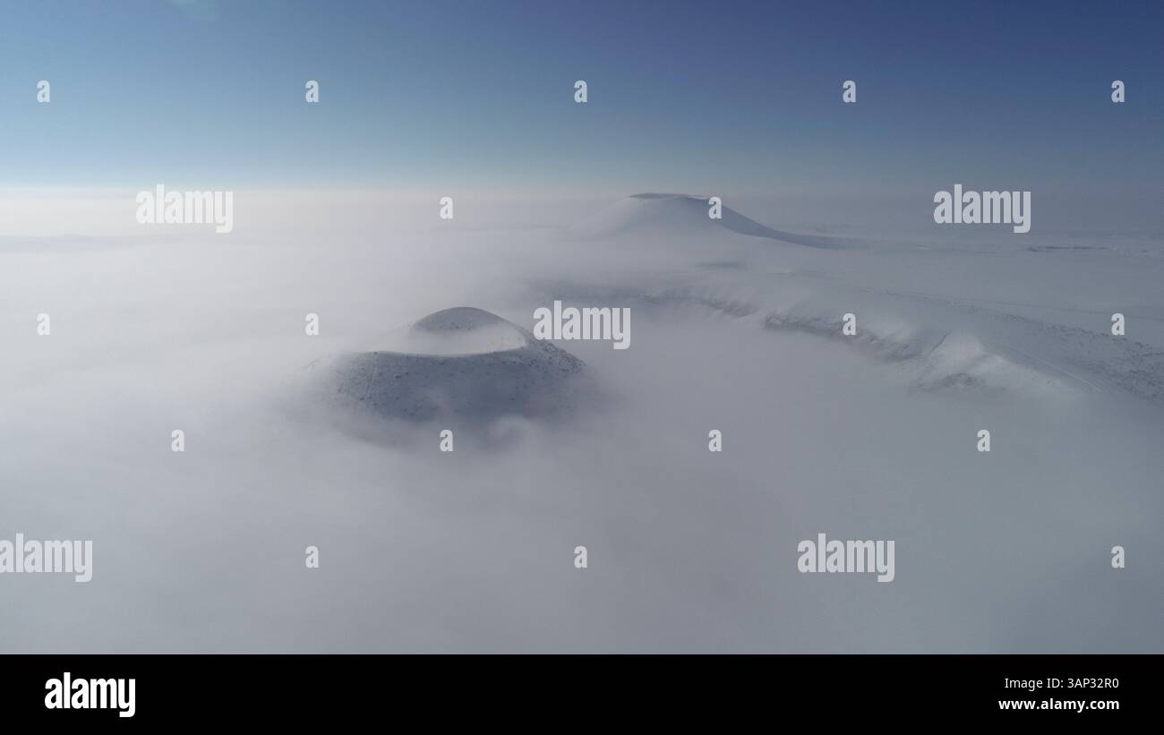 Aerial view of a beautiful snow-capped mountain peak surrounded by fog ...