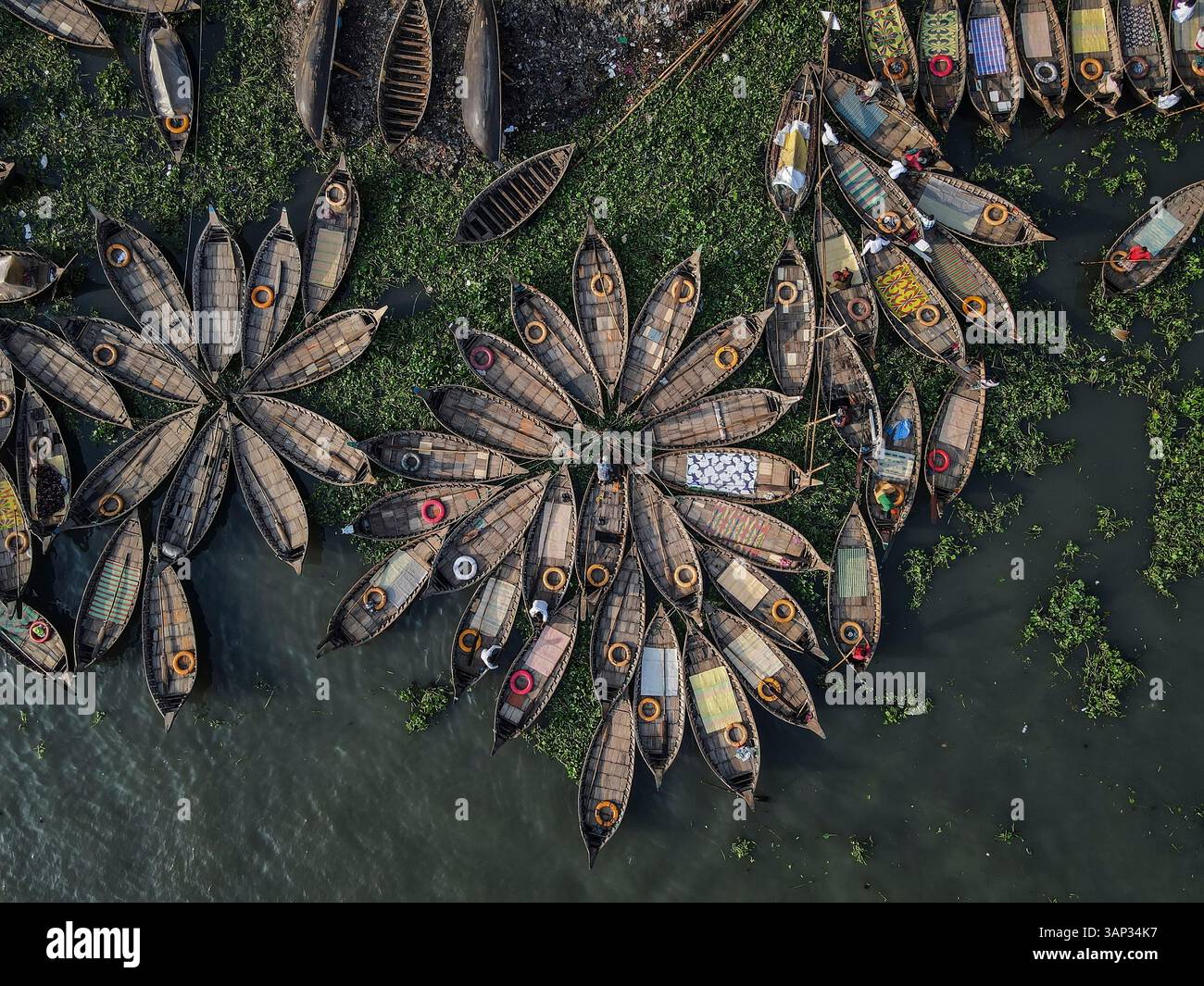 Aerial view of traditional wooden boats on the polluted Buriganga river with people docked ...