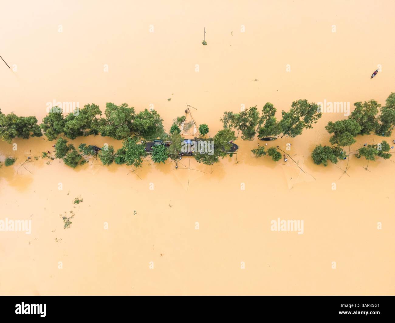 Aerial view of a flooded village with submerged houses and a road surrounded by trees ...