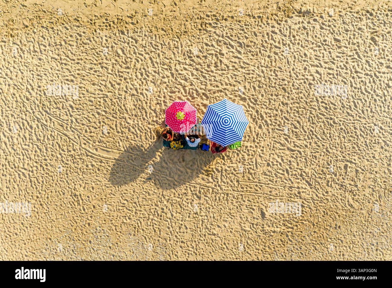 Aerial view of two umbrellas on the beach and people seating on their ...