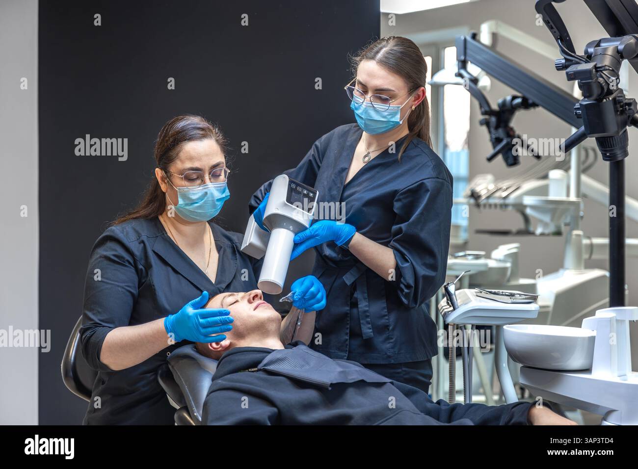 A team of dentists treats a patient's teeth using modern equipment ...