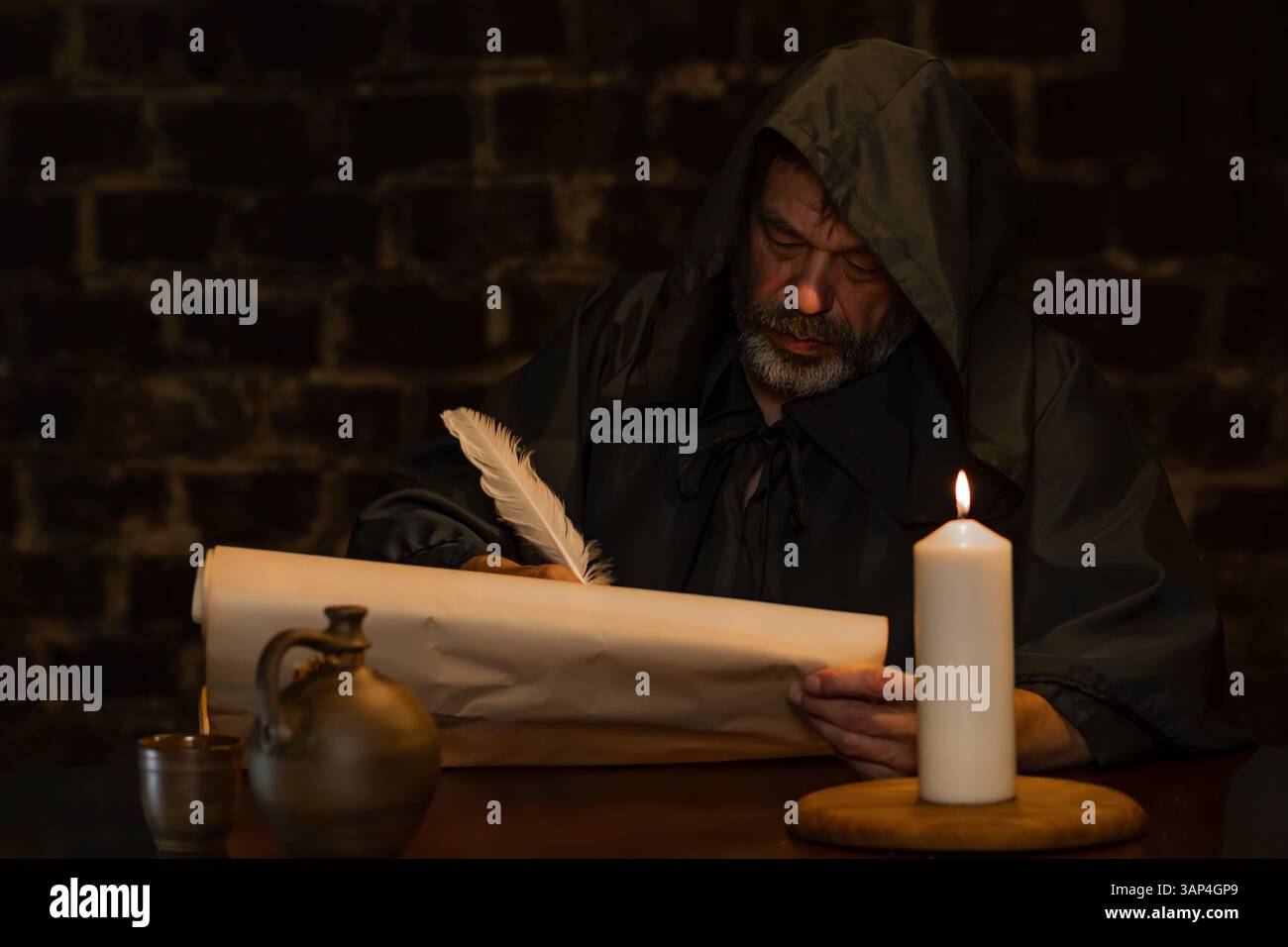 A medieval monk writes with a quill pen on parchment by candlelight ...