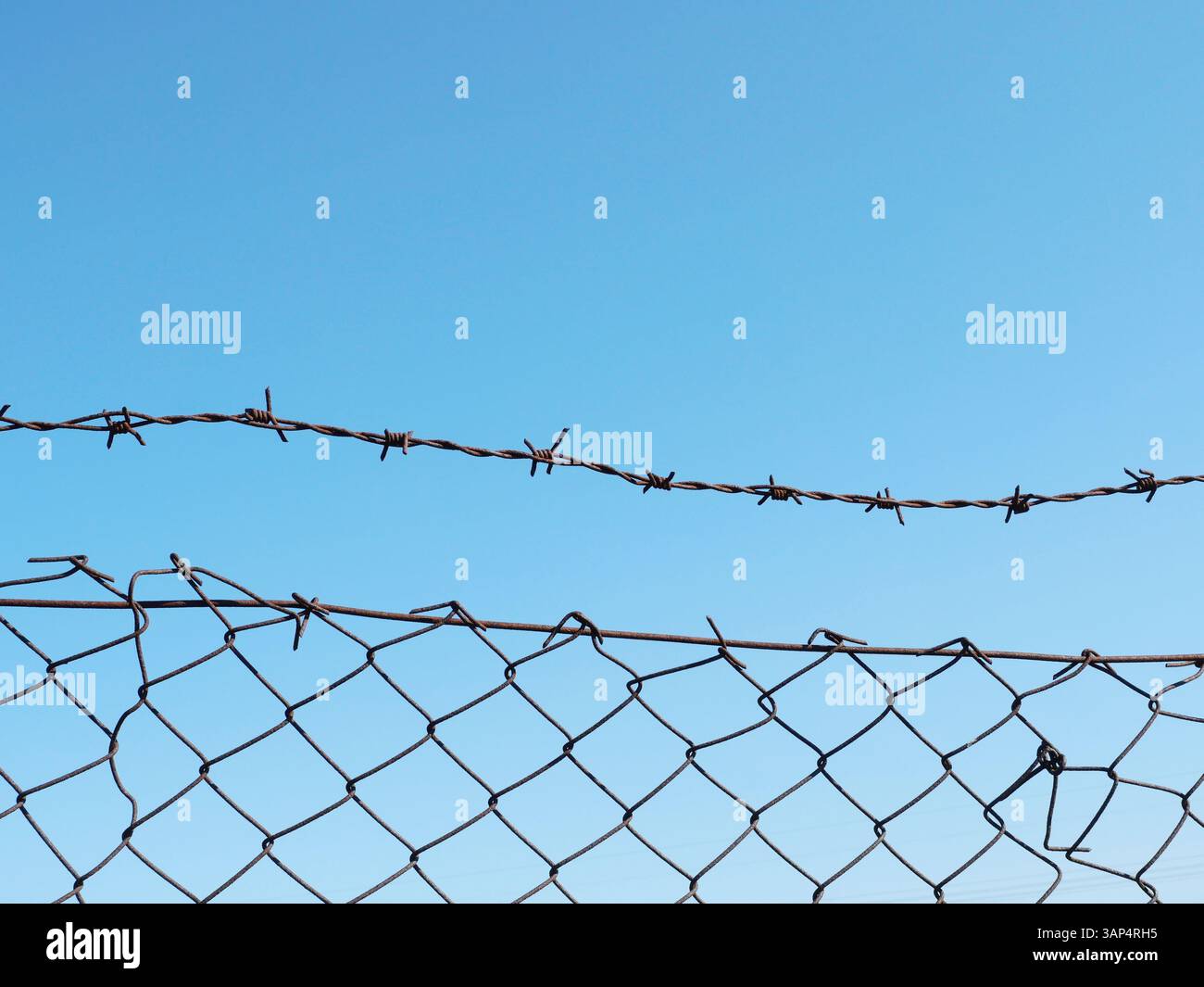 A weathered wire mesh fence with barbed wire secures an unused pasture ...