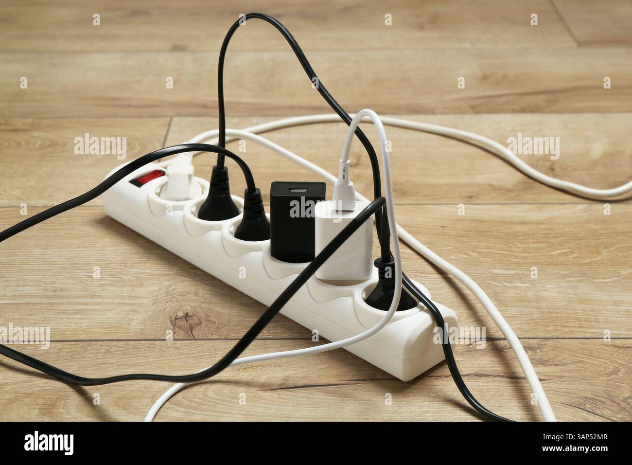 Extension power board overloaded with plugs on wooden floor, closeup ...