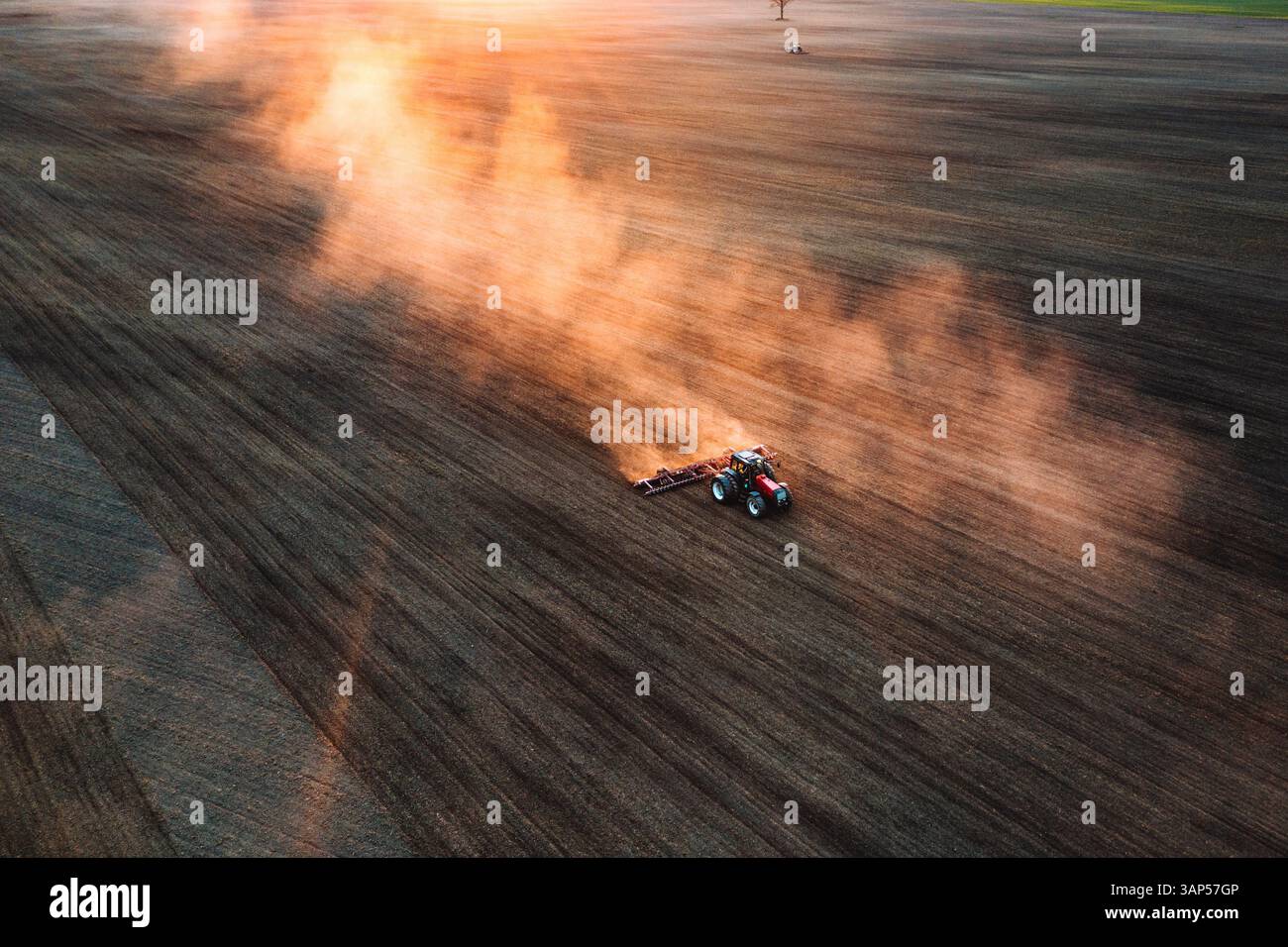 Aerial view of soil fields harrowing tractor and golden dust clouds ...