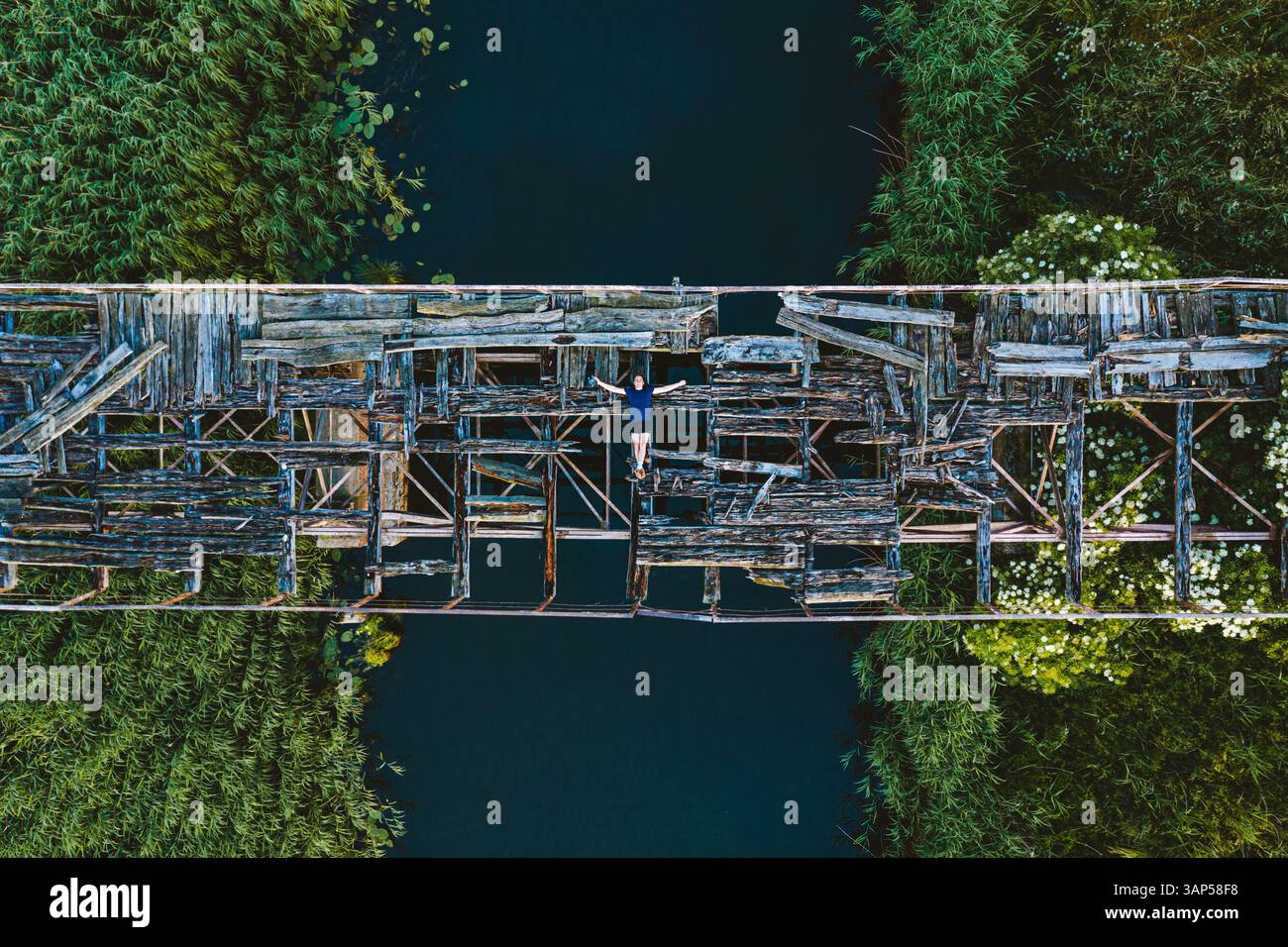 Aerial view of person lying down on old wooden collapsed bridge in ...