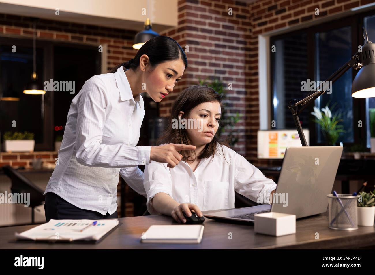 Two professional women in a late night office meeting, comparing notes ...