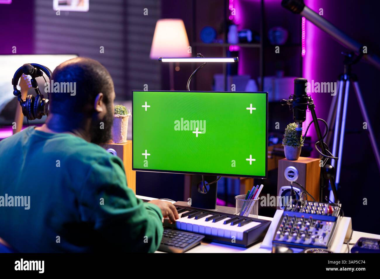 Musician operates on midi controller piano keys next to mockup screen ...