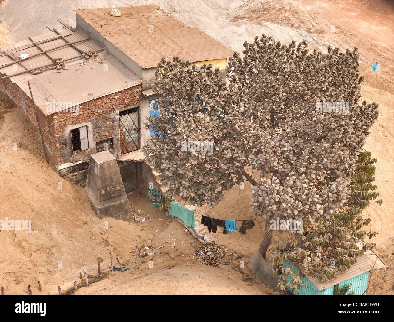 Aerial view of a sand pit and rustic houses surrounded by trees in a dusty environment, Dhaka ...