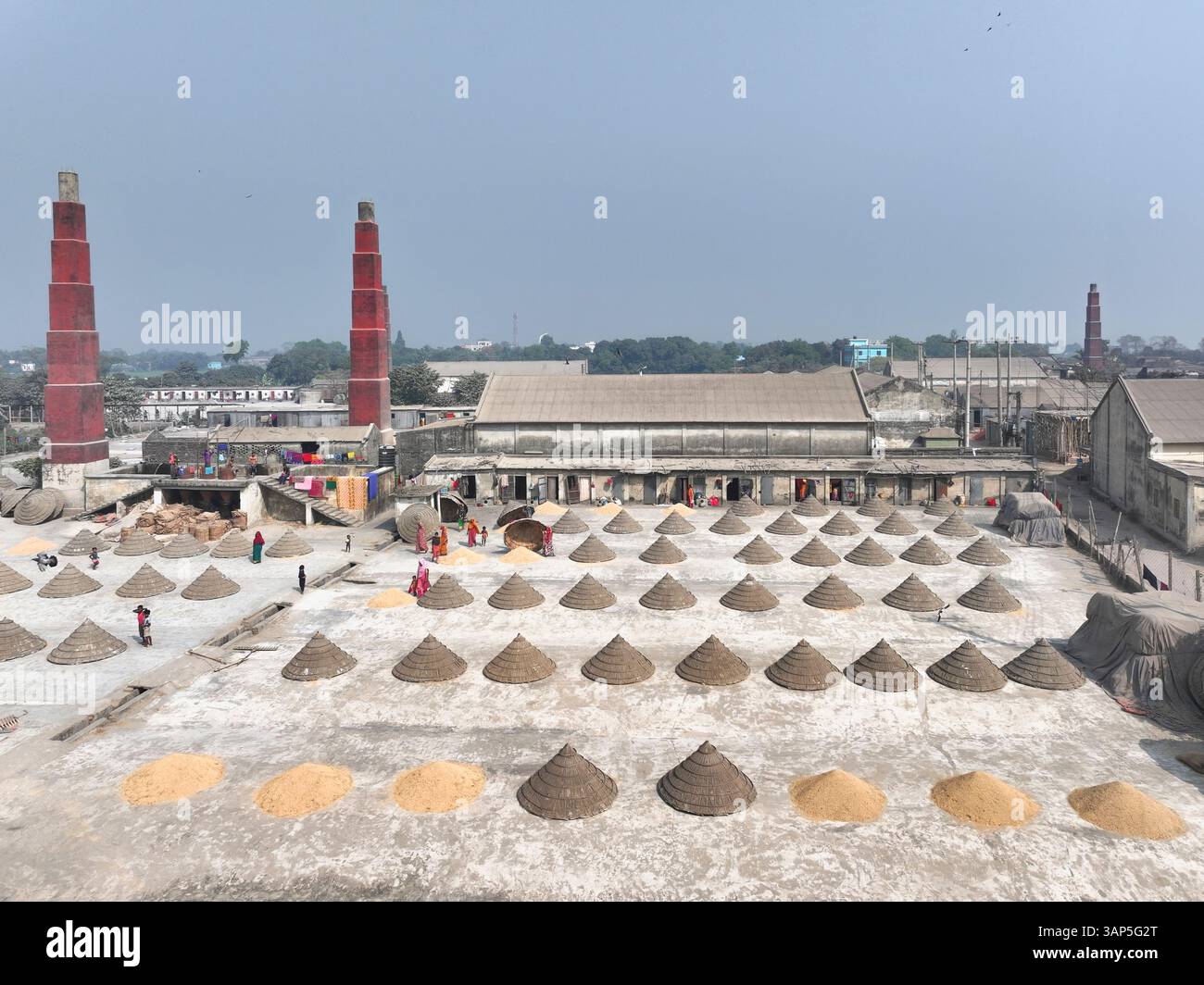 Aerial view of rice mill with workers, children, and women amidst heaps ...