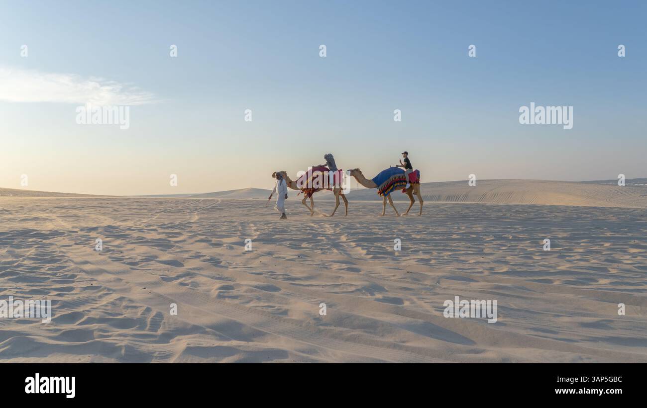 Doha, Qatar, February 24, 2025: A group of people riding camels through ...