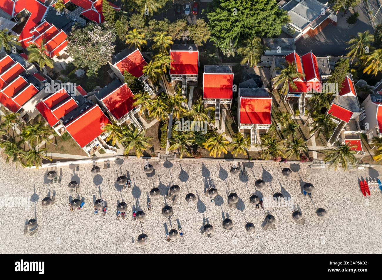 Aerial view of a beachfront hotel with red roofs and parasols throwing ...