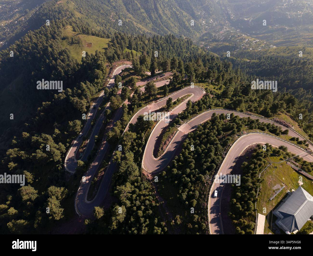 Aerial view of winding road through lush forest and majestic mountains ...