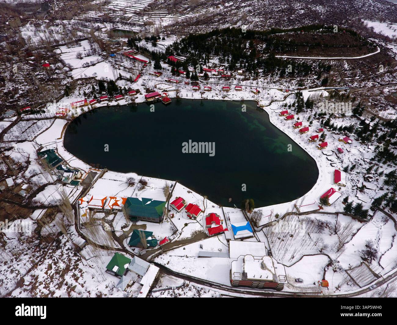 Aerial view of snowy village with frozen lake and snow-capped mountains ...