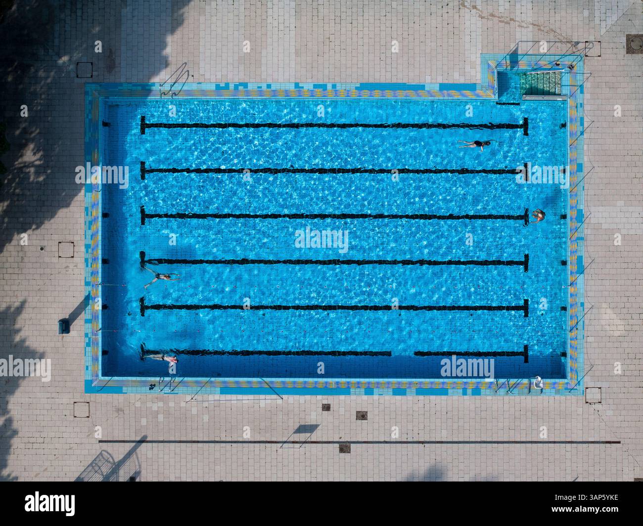 Aerial view of a vibrant public pool with people swimming under sunny ...