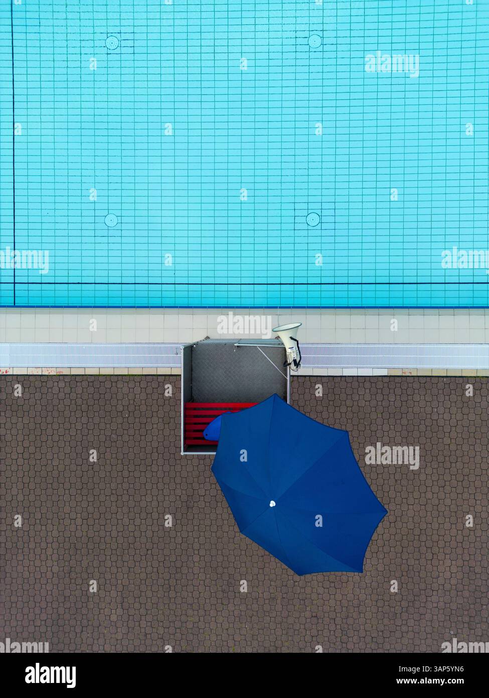 Aerial view of a vibrant public pool with blue umbrellas and geometric ...