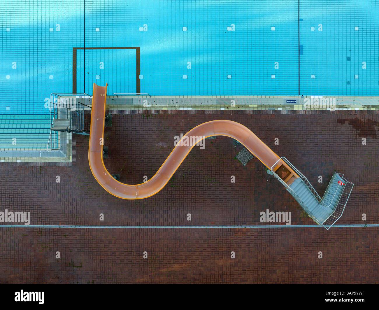 Aerial view of a vibrant public pool with a curved slide and geometric ...