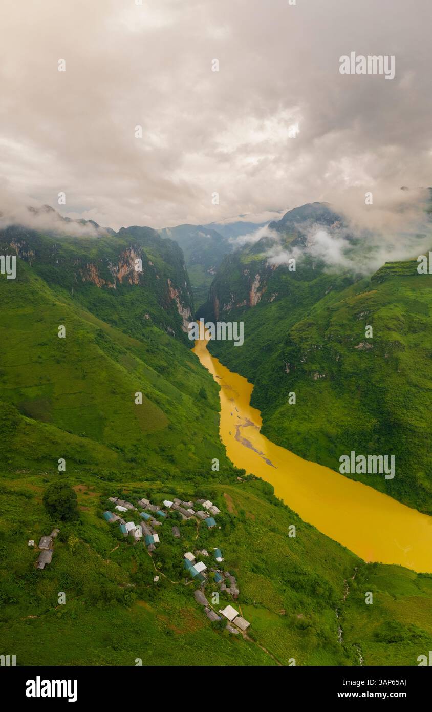 Aerial view of remote village nestled in lush valley with winding nho ...