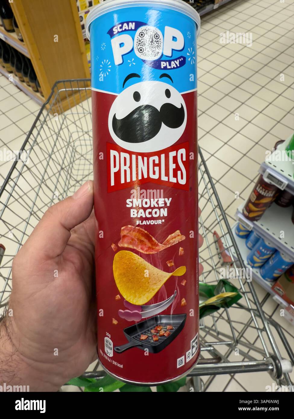 Hand holding a tube of Pringles Smokey Bacon flavour potato chips in a ...