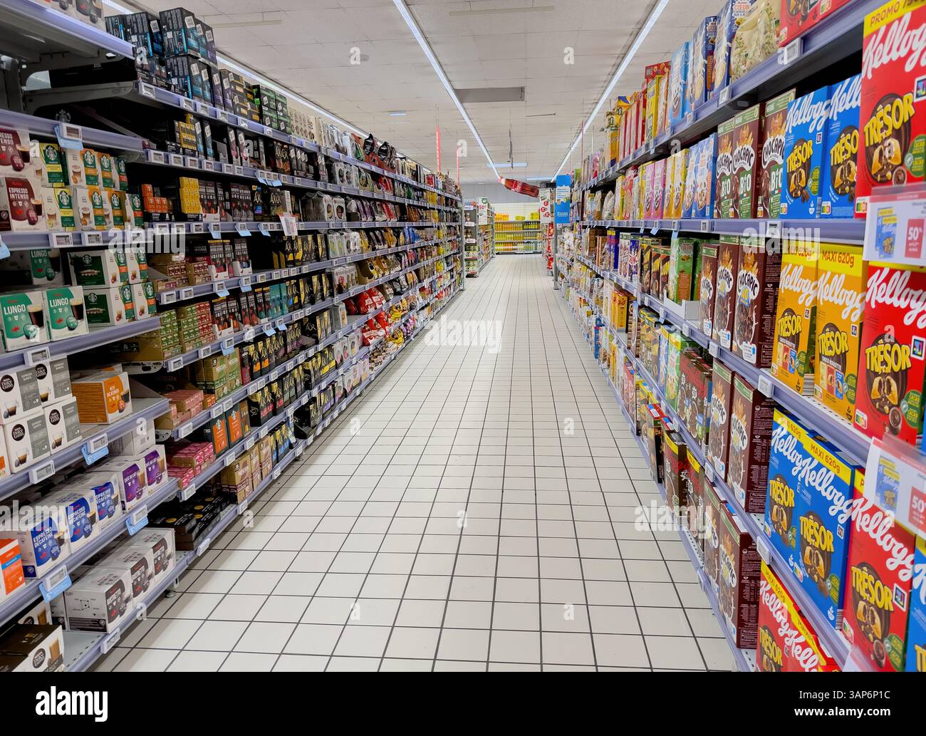 Long supermarket aisle with shelves full of products like coffee capsules and breakfast cereals ...