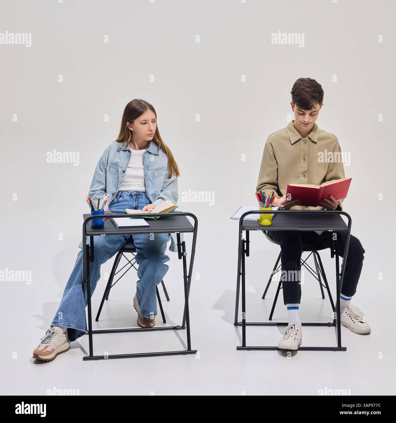Teen boy and girl sitting at desks in classroom, reading textbooks ...