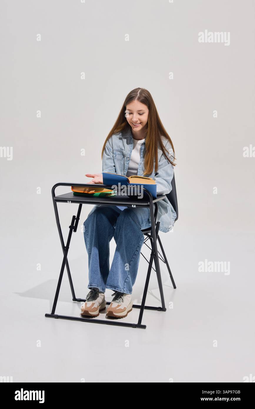 Girl in denim jacket sits alone at desk, smiling and presenting ideas ...