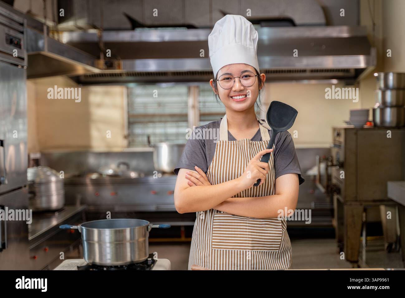 Smiling young female chef in professional kitchen attire, holding a ...