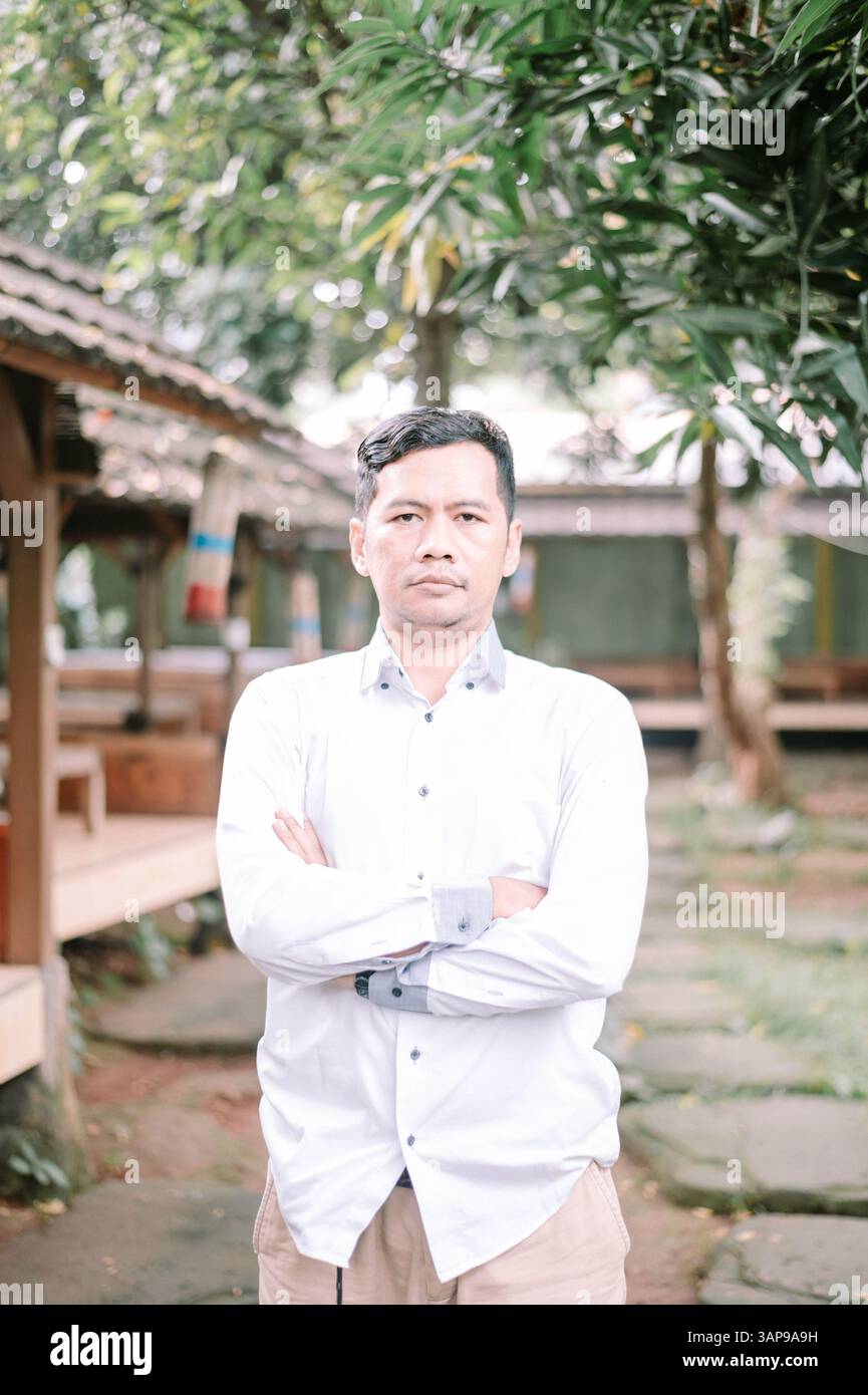 Confident Asian man stands with folded arms outdoors, showing ...