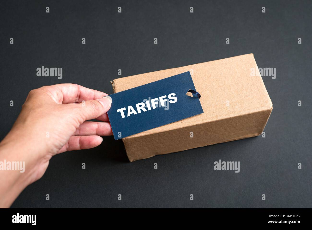 Hand holding tag with tariffs message, on top of cardboard package ...
