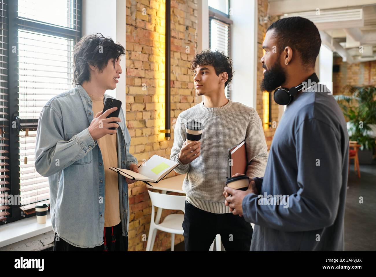 Three colleagues engage in an animated discussion while holding coffee ...
