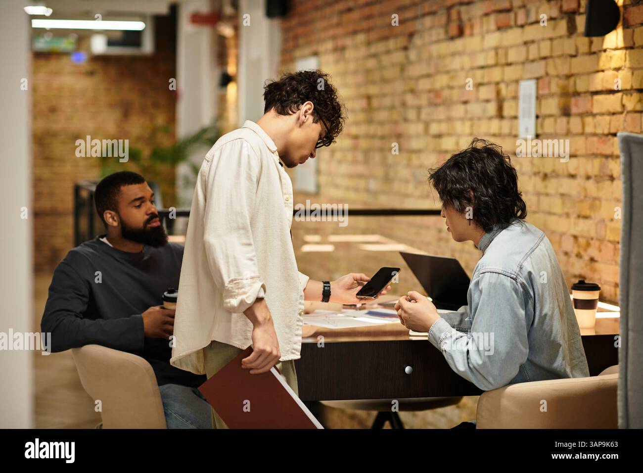 Three people discuss ideas and technology around a table in an office ...
