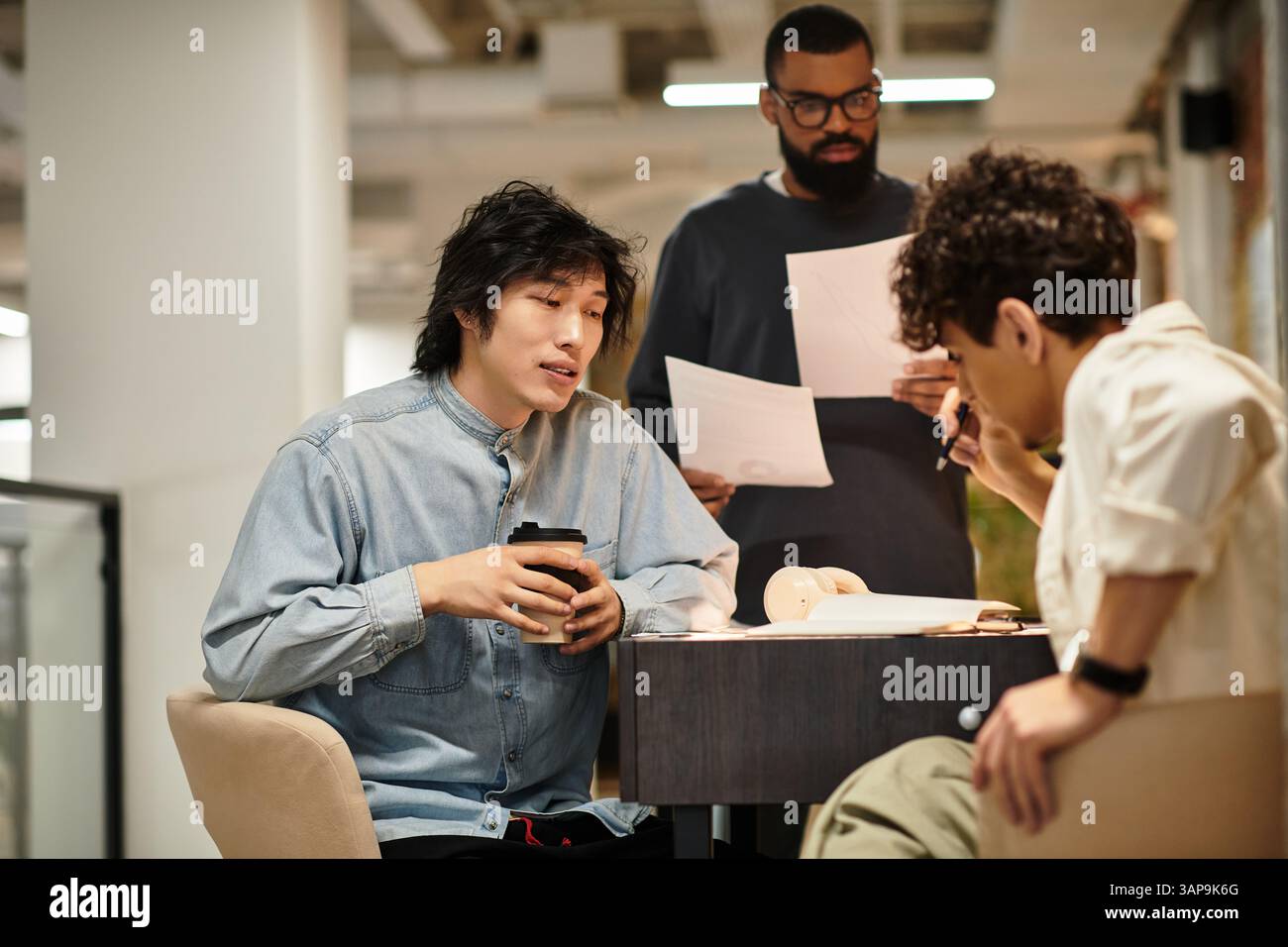Three people discuss ideas and review documents at a table in a modern ...