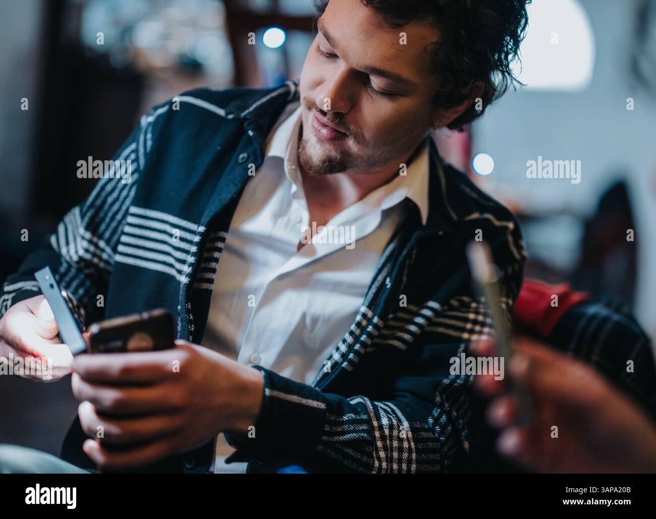 Casually dressed young man using a smartphone, sitting indoors with ...
