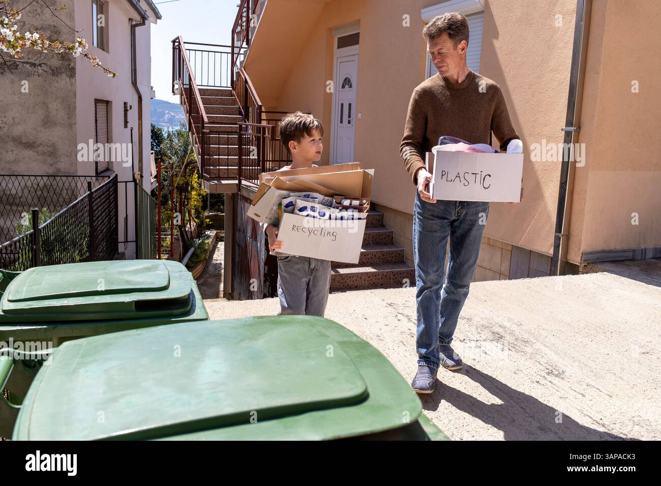 Father and son talk while carrying sorted waste to recycling bins Stock ...