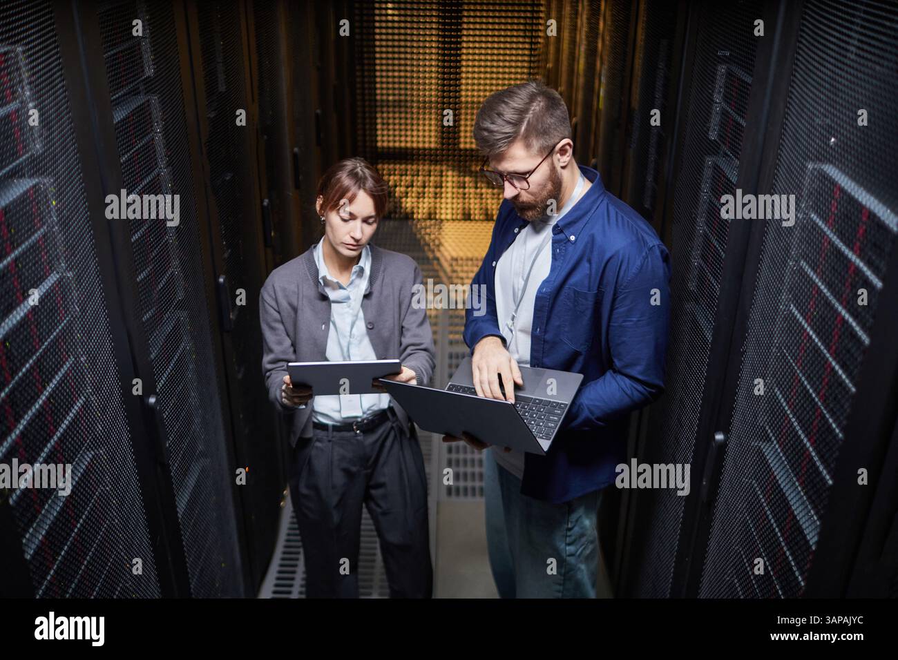 Two IT professionals collaborating in data center while using laptop ...