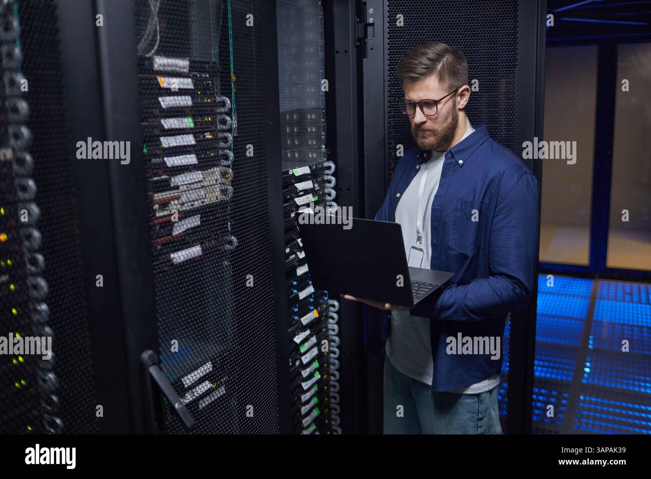 Male IT technician standing in modern server room holding laptop ...