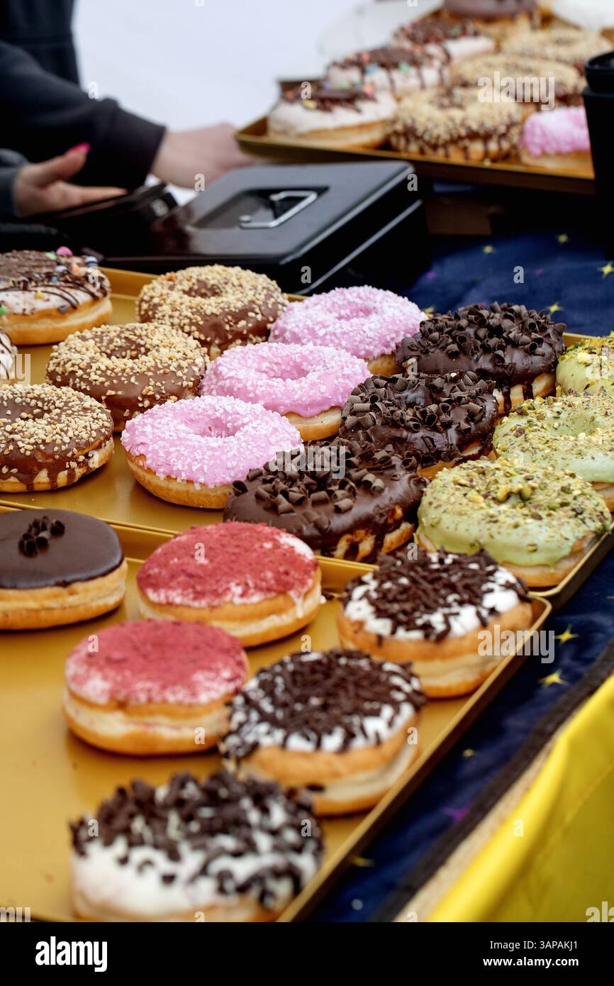 Variety of glazed donuts with different toppings arranged on gold tray ...