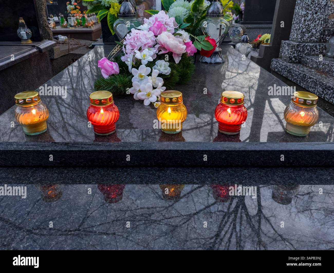 Glowing mourning candles, red, yellow and white sit on a dark granite ...