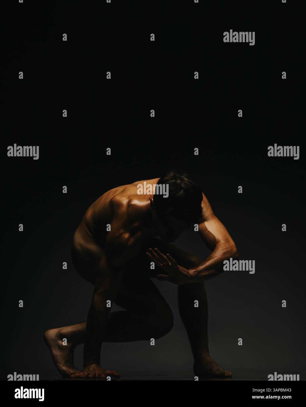 Athletic man striking a dramatic pose under focused studio lighting ...