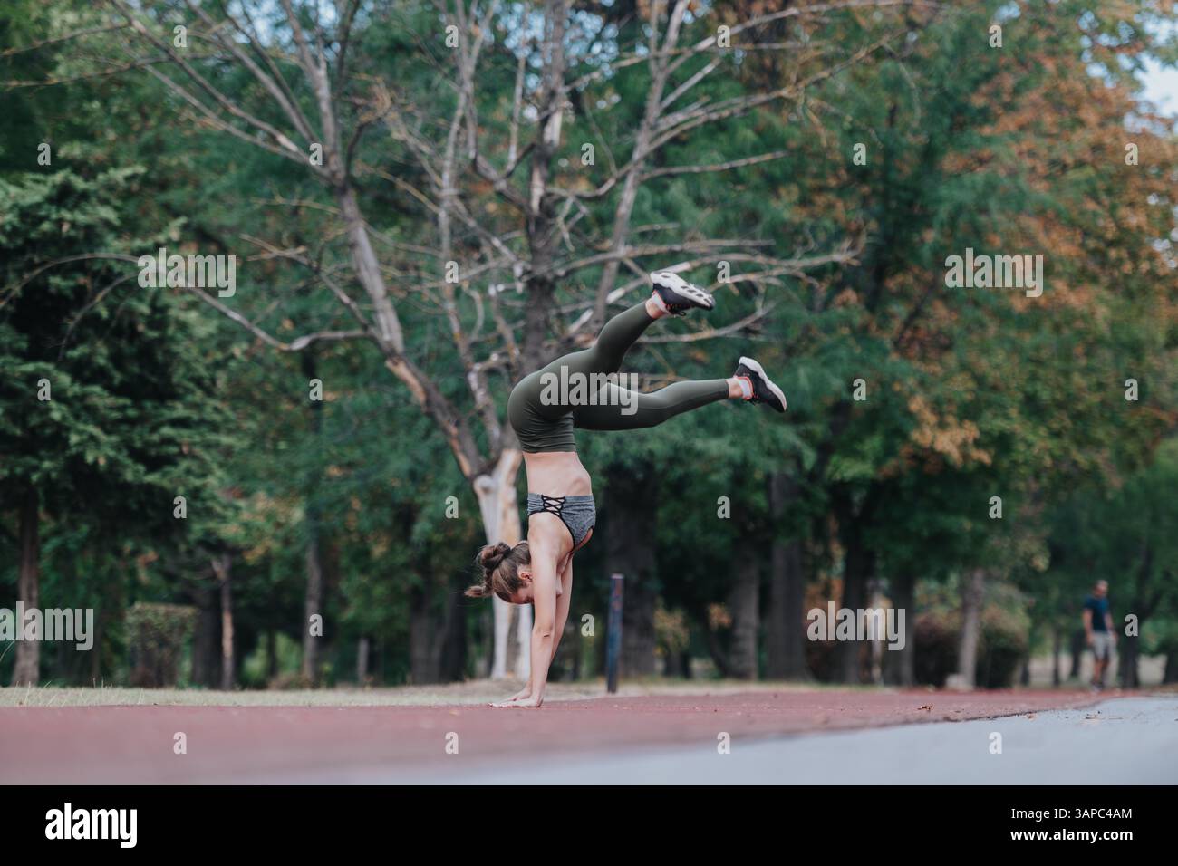 Young woman performing a handstand on a park path amid lush greenery ...