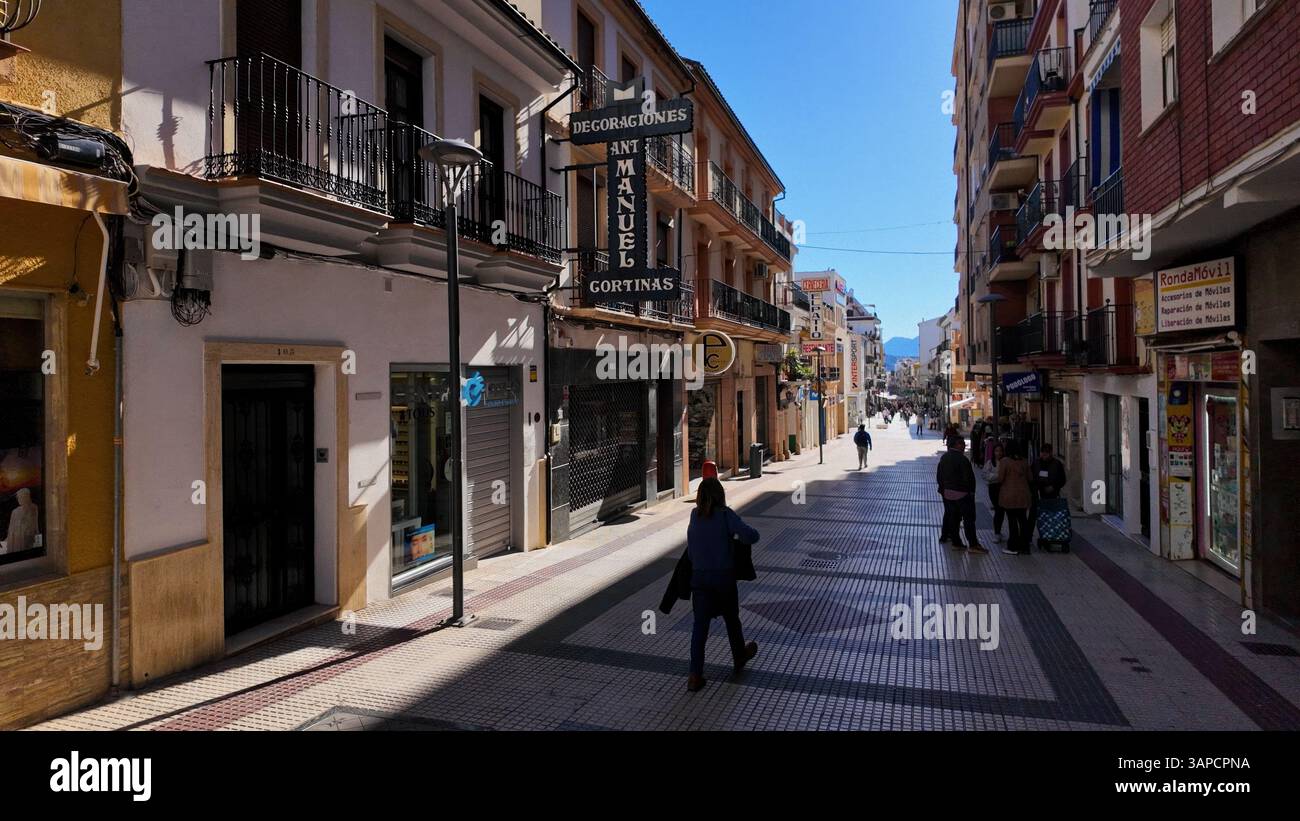 Tourists and locals walking down a pedestrian shopping street in Ronda ...