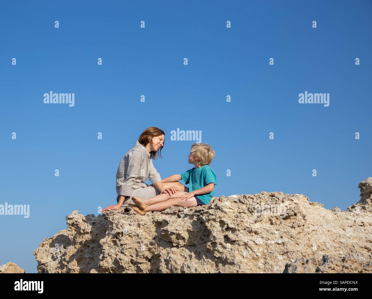 Mom and son barefoot on rock against the blue sky on a sunny day ...