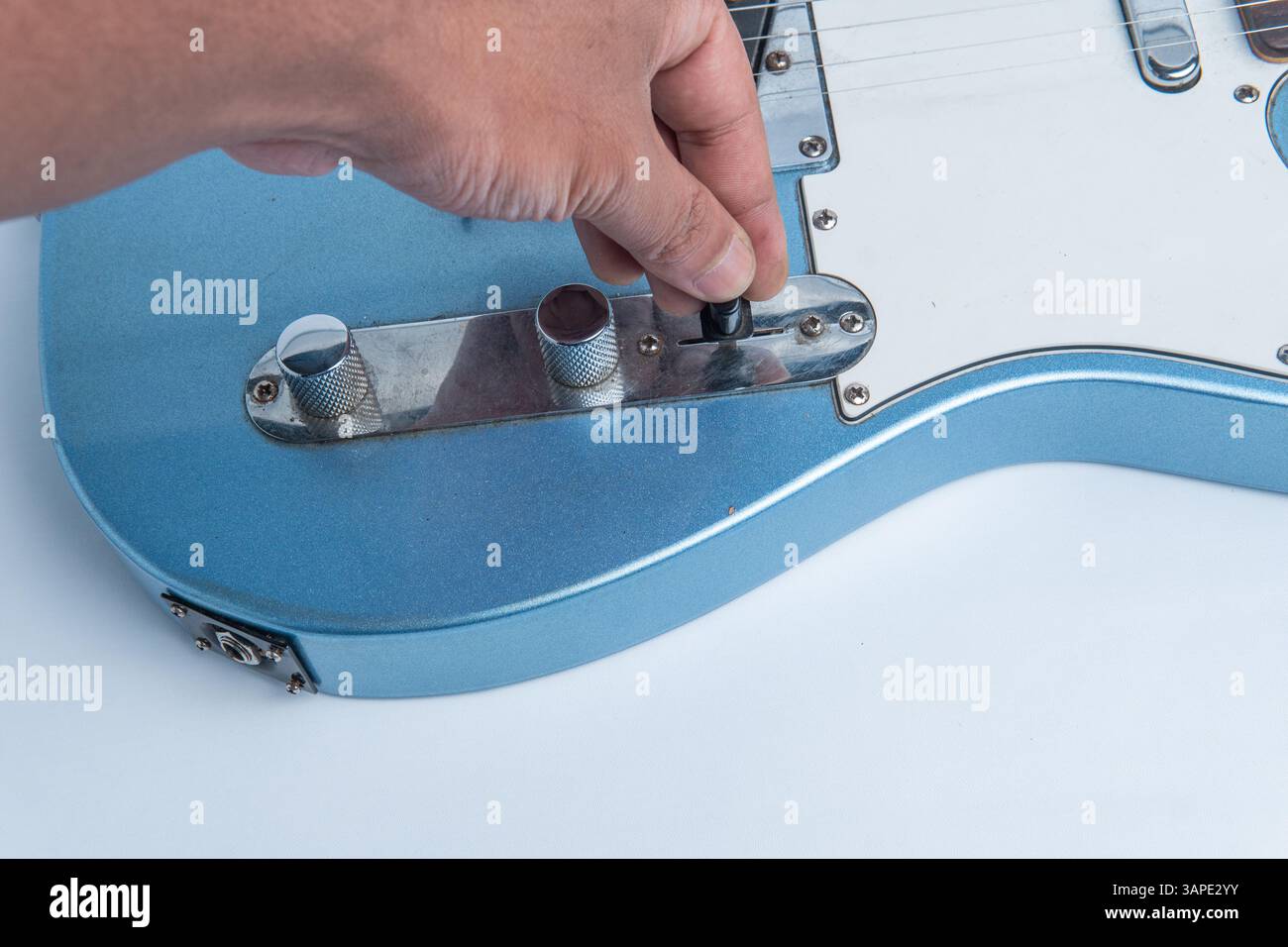 A close-up shot of a hand adjusting the pickup switch on a blue ...