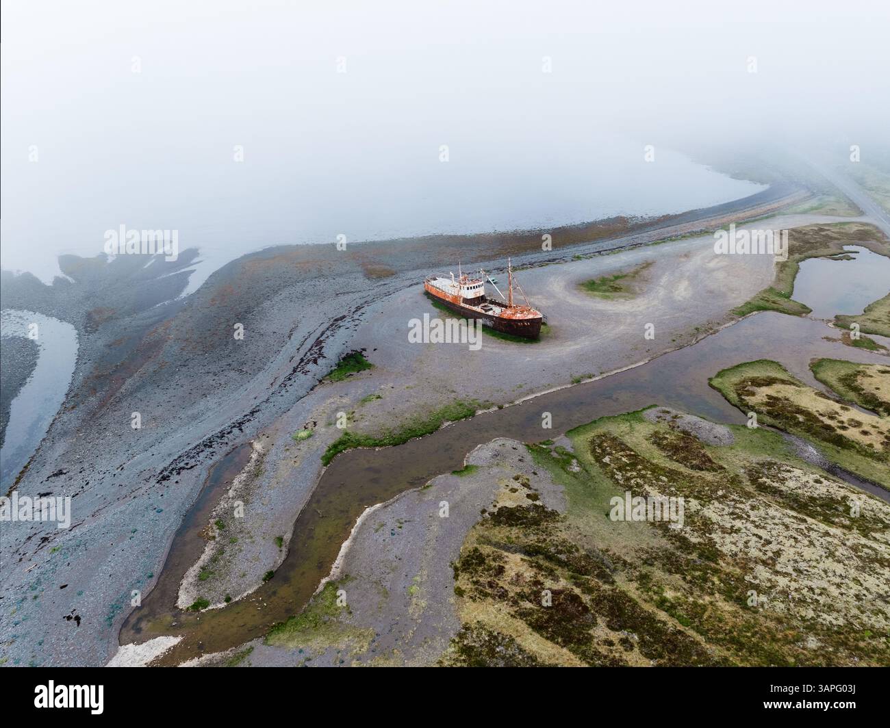 Aerial view of a rusted shipwreck stranded on a misty Icelandic shore ...
