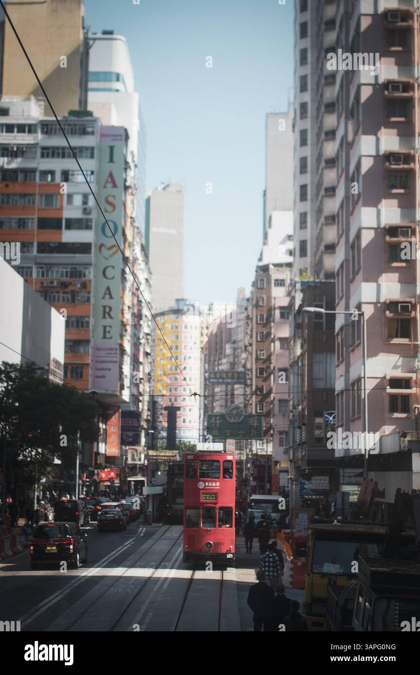 A classic red double-decker tram moves through a busy street lined with ...