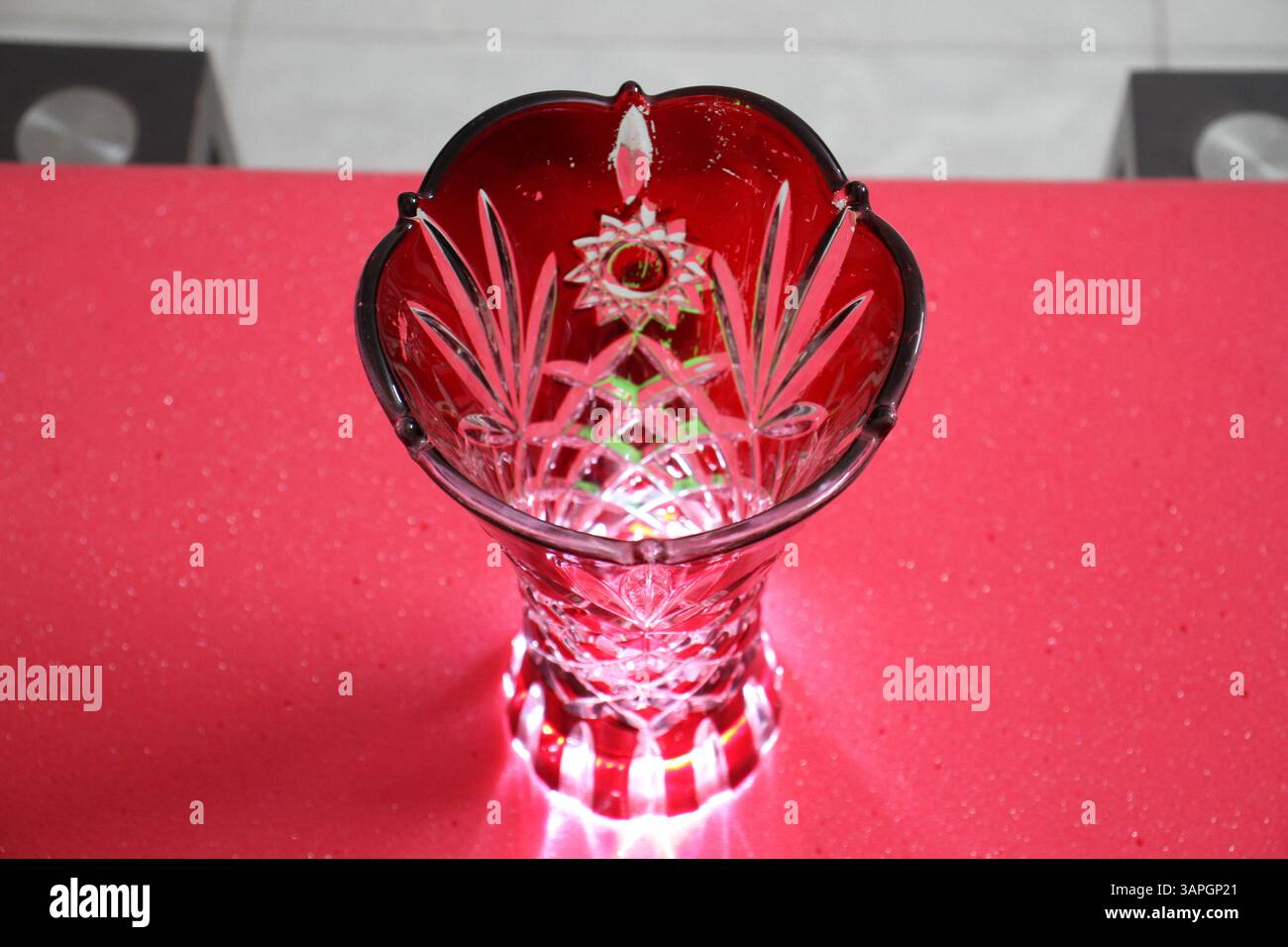 A glass made red colored flower vase with bright light stands on table ...