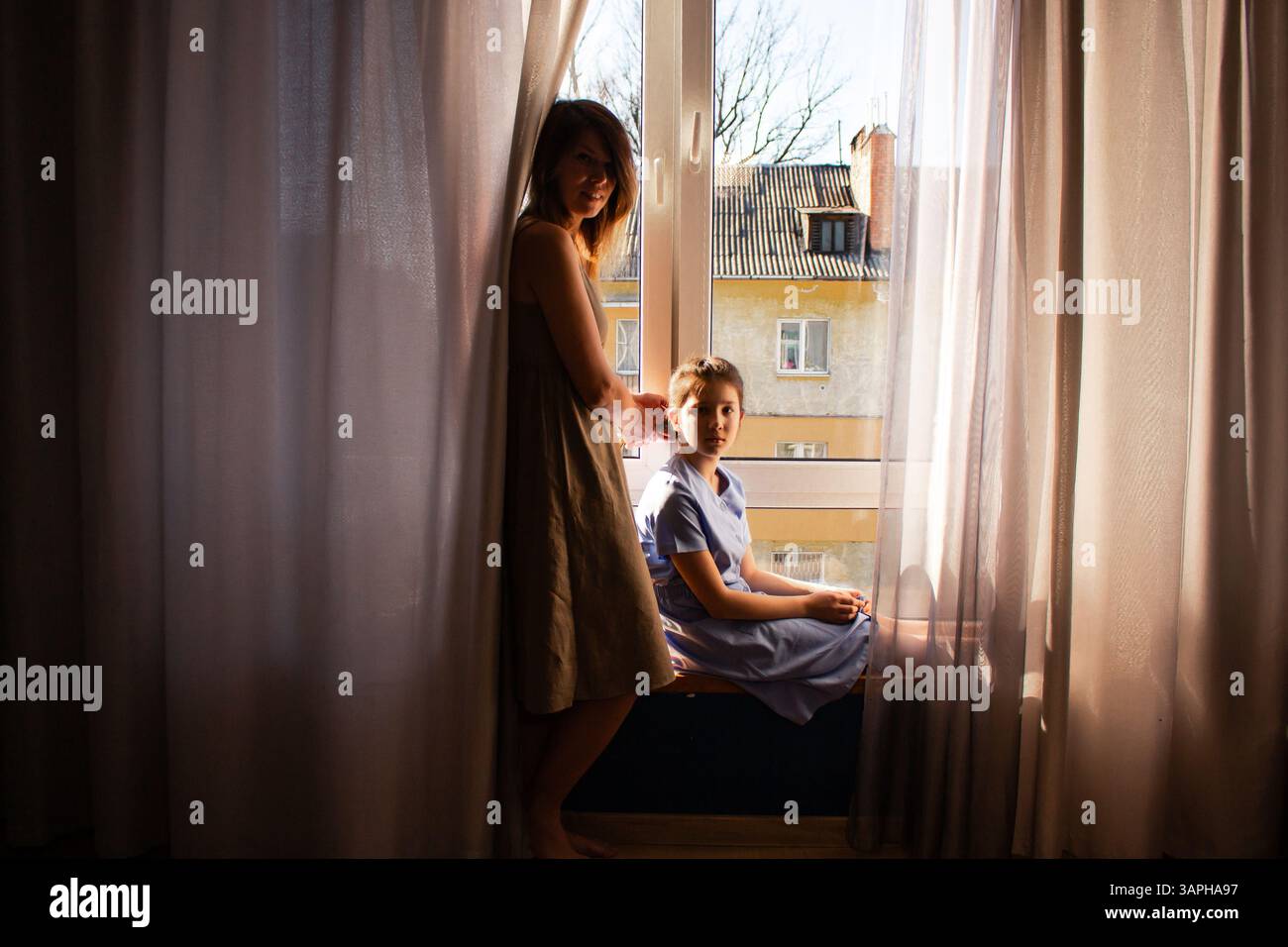 Mother braiding daughter's hair in cozy home setting. Tender parenting ...