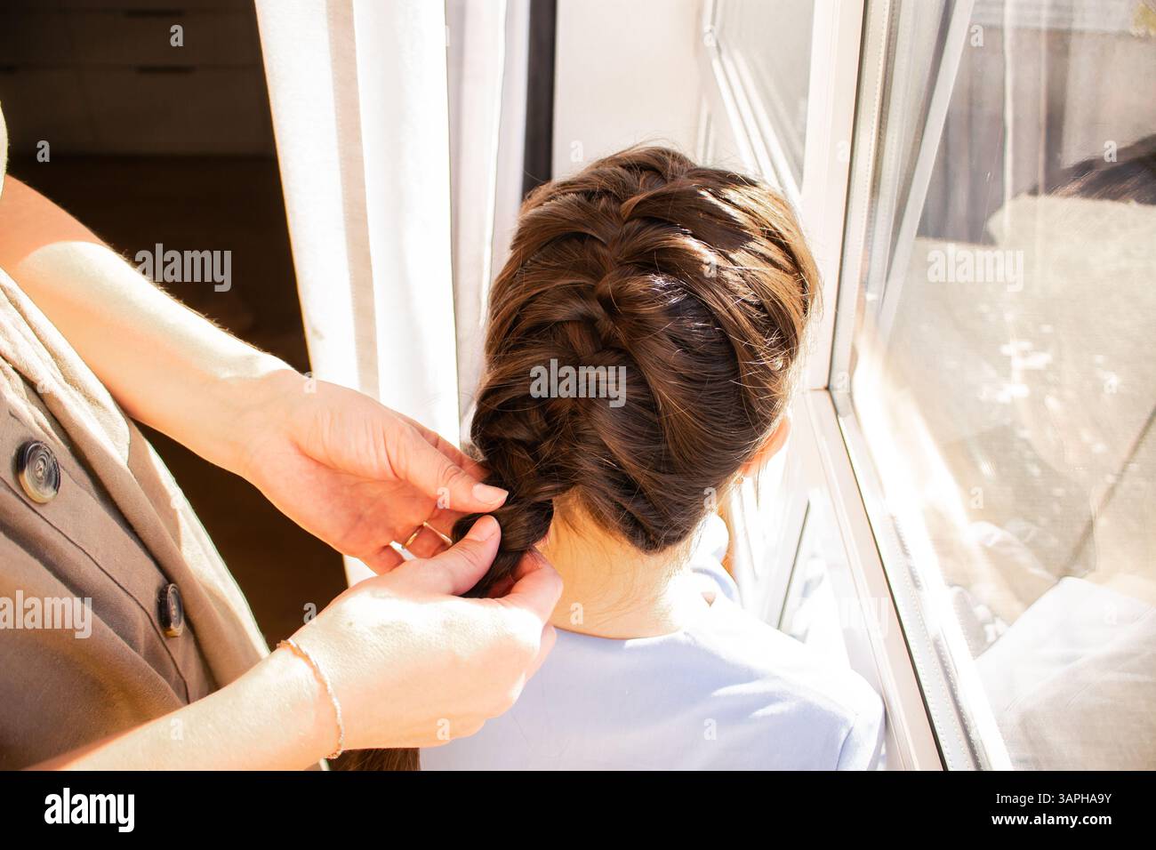 Mother braiding daughter's hair in cozy home setting. Tender parenting moment showing love ...