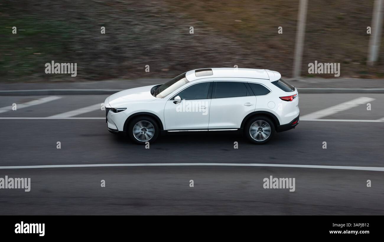 White Mazda CX-9 driving on a road. Side view of japanese crossover SUV ...